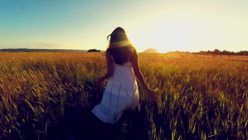 Young Woman In White Sun Dress Walking Through Grassy Field At Sunset ...